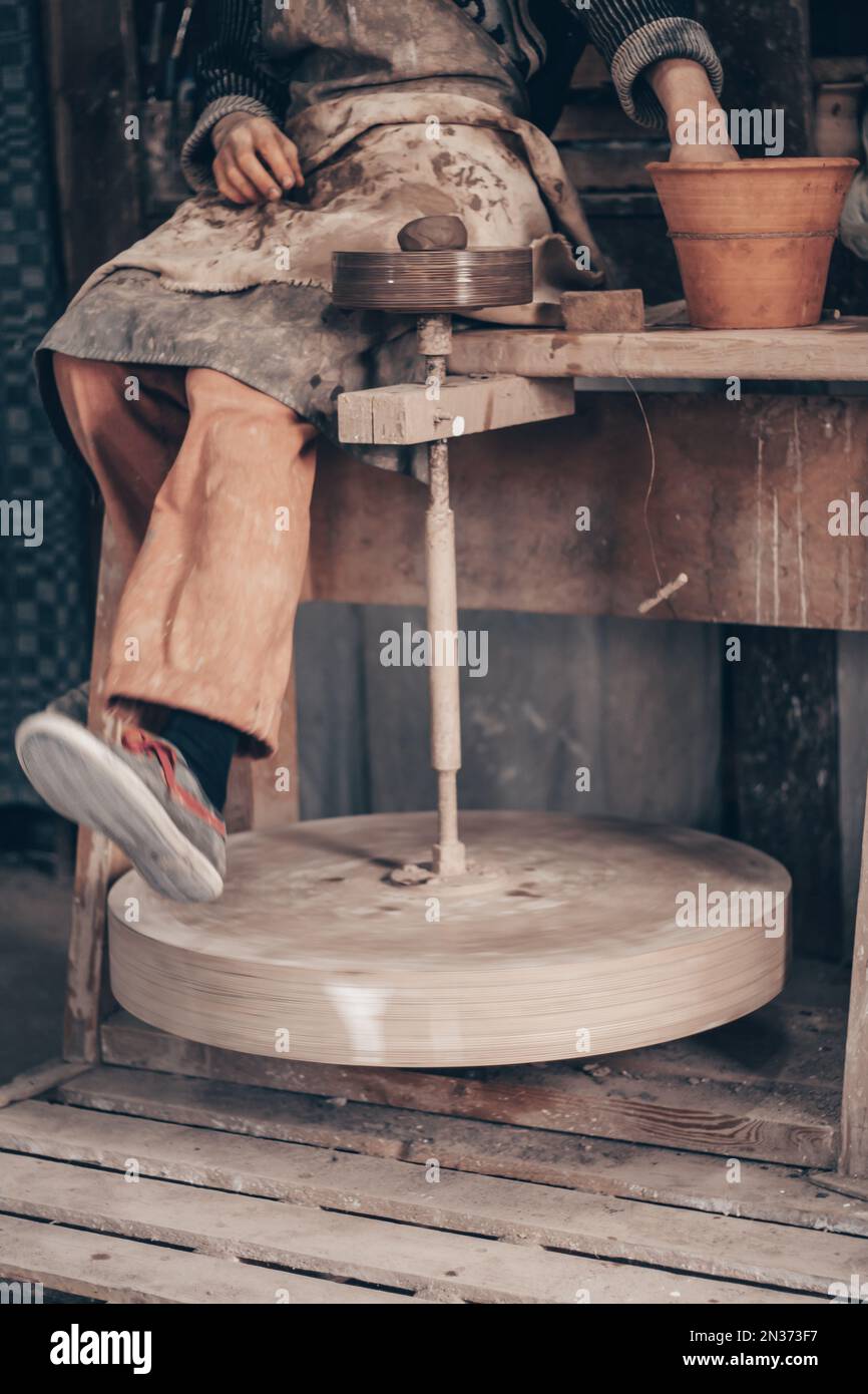 Craftsman in dirty working clothes sit on potter machine and spin wheel ...