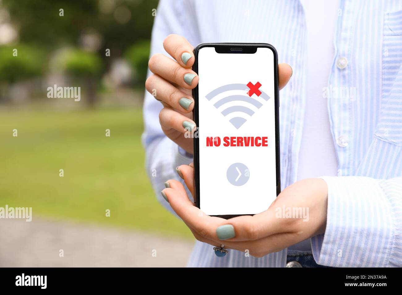 Woman holding mobile phone with text NO SERVICE on screen outdoors ...
