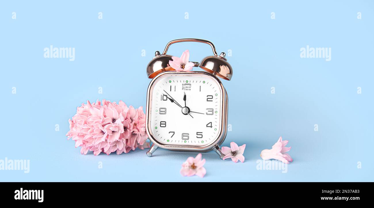 Alarm clock and flowers on light blue background. Spring time Stock ...