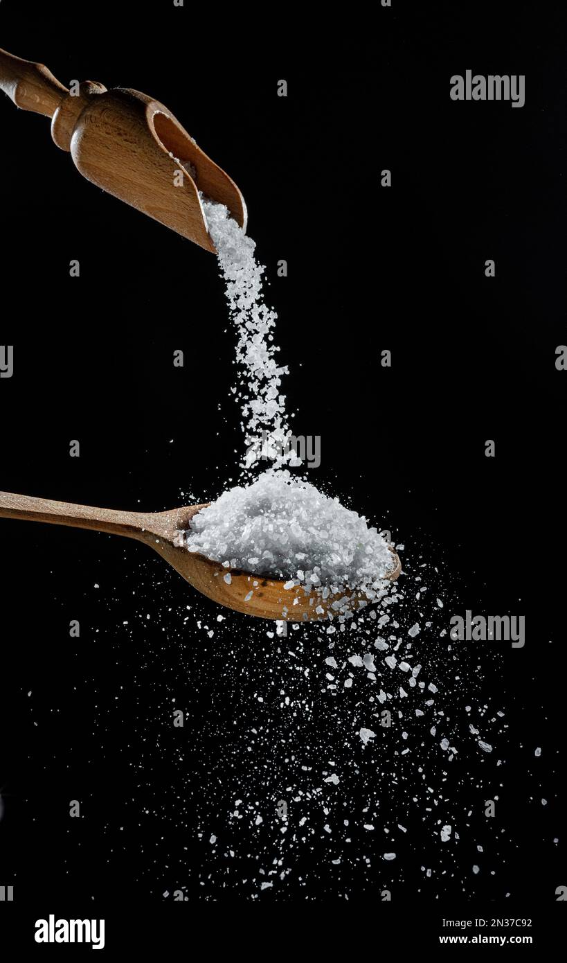 Edible salt crystals falling down into the wooden spoon at black ...