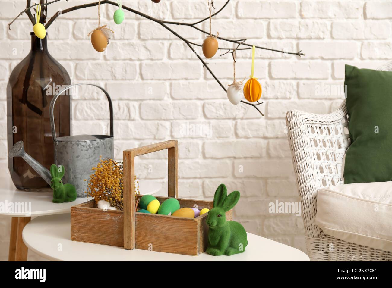 Vase with tree branches, Easter eggs, box and rabbits on tables in ...