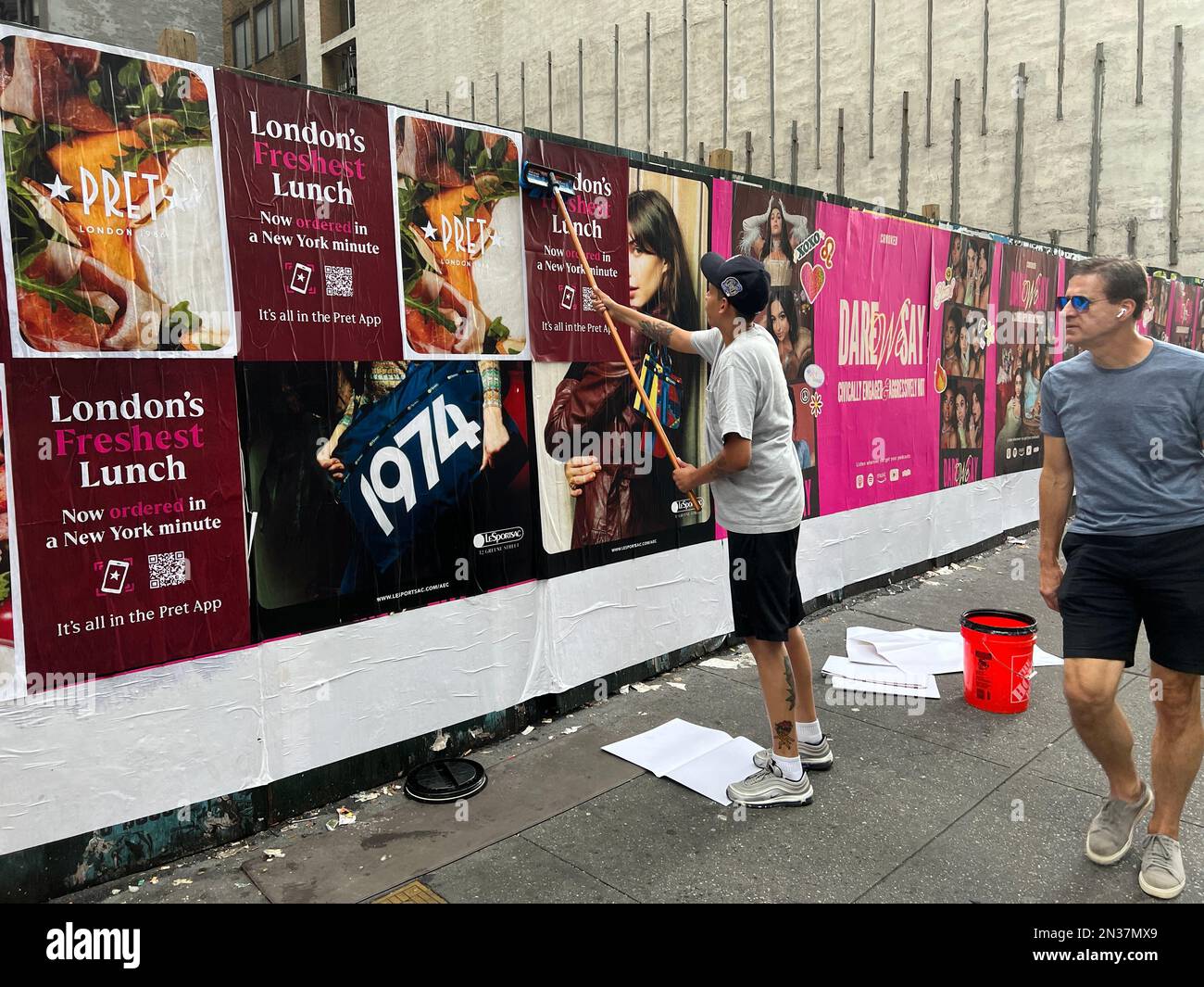 Worker puts up advertising posters on a temporary construction site ...