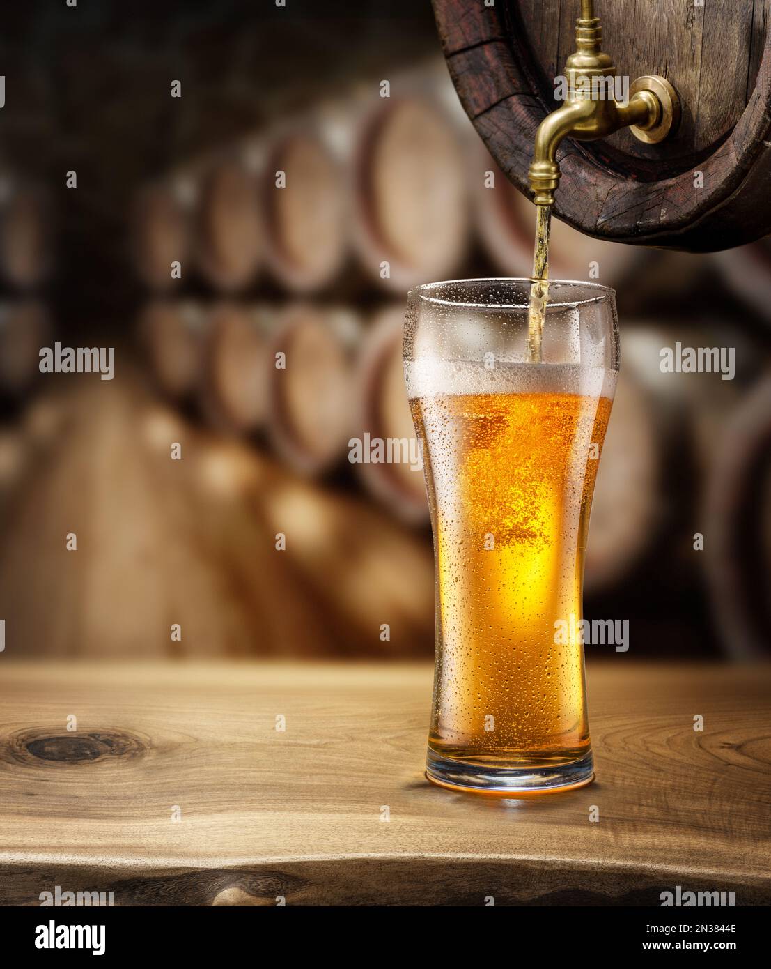 Pouring beer into a glass from wooden barrel. Blurred brewery cellar at ...