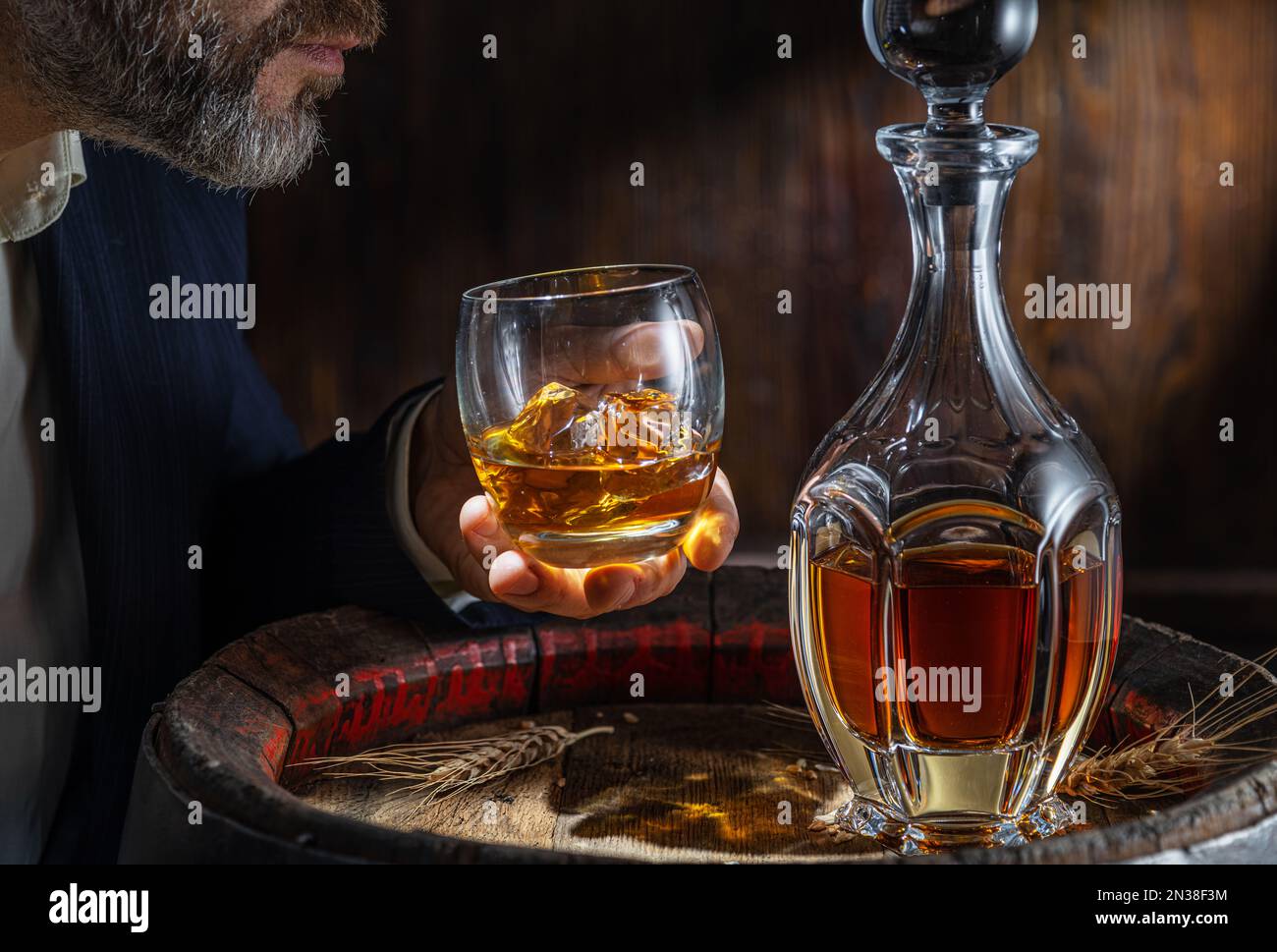 Whisky tasting. Man sits in front of a barrel with a decanter and a ...