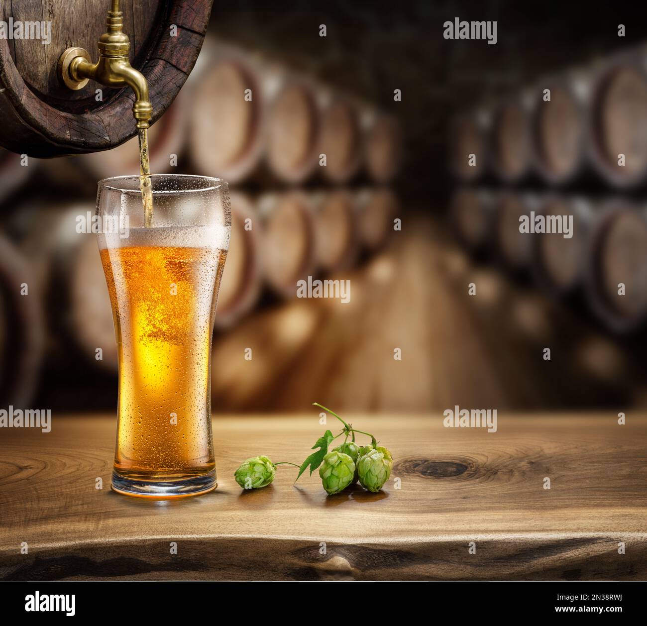 Pouring beer into a glass from wooden barrel. Blurred brewery cellar at ...