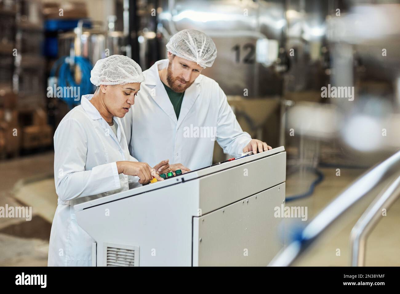 Portrait of two workers wearing lab coats operating equipment at food ...