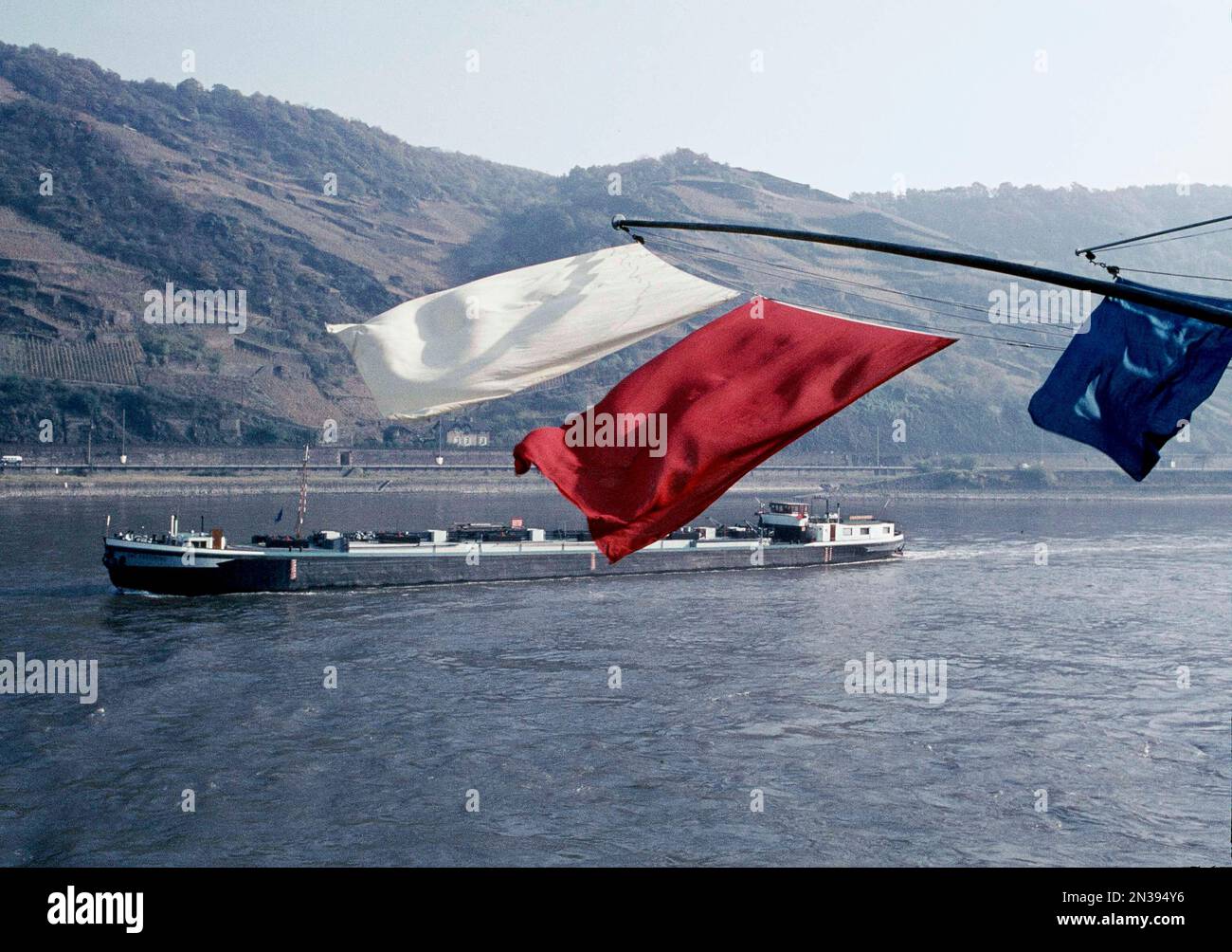 Flags flutter in the breeze as a barge on the Rhine River passes the ...