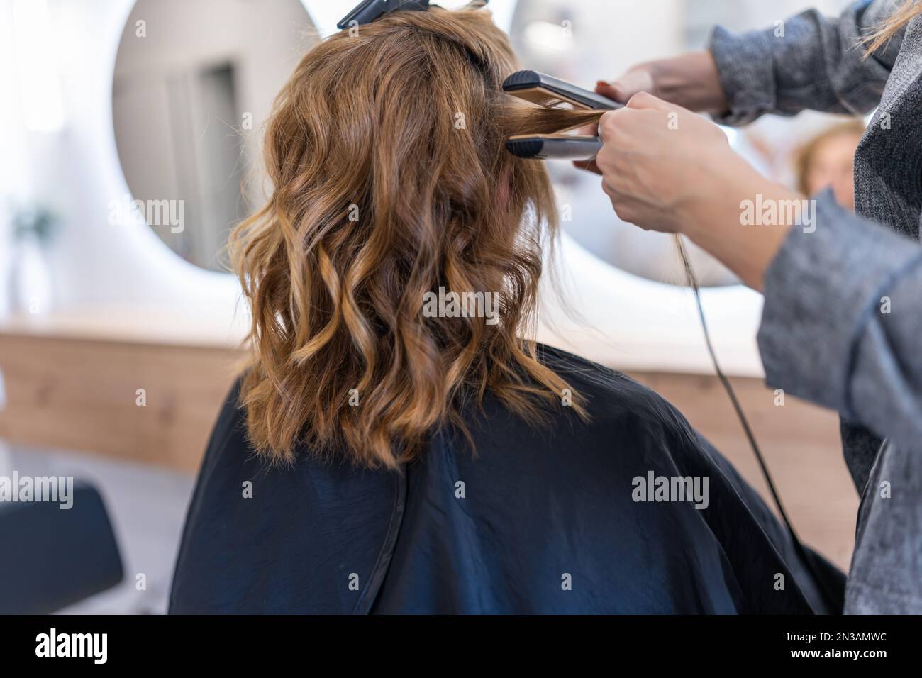 Anonymous stylist curling hair of unrecognizable client with ...