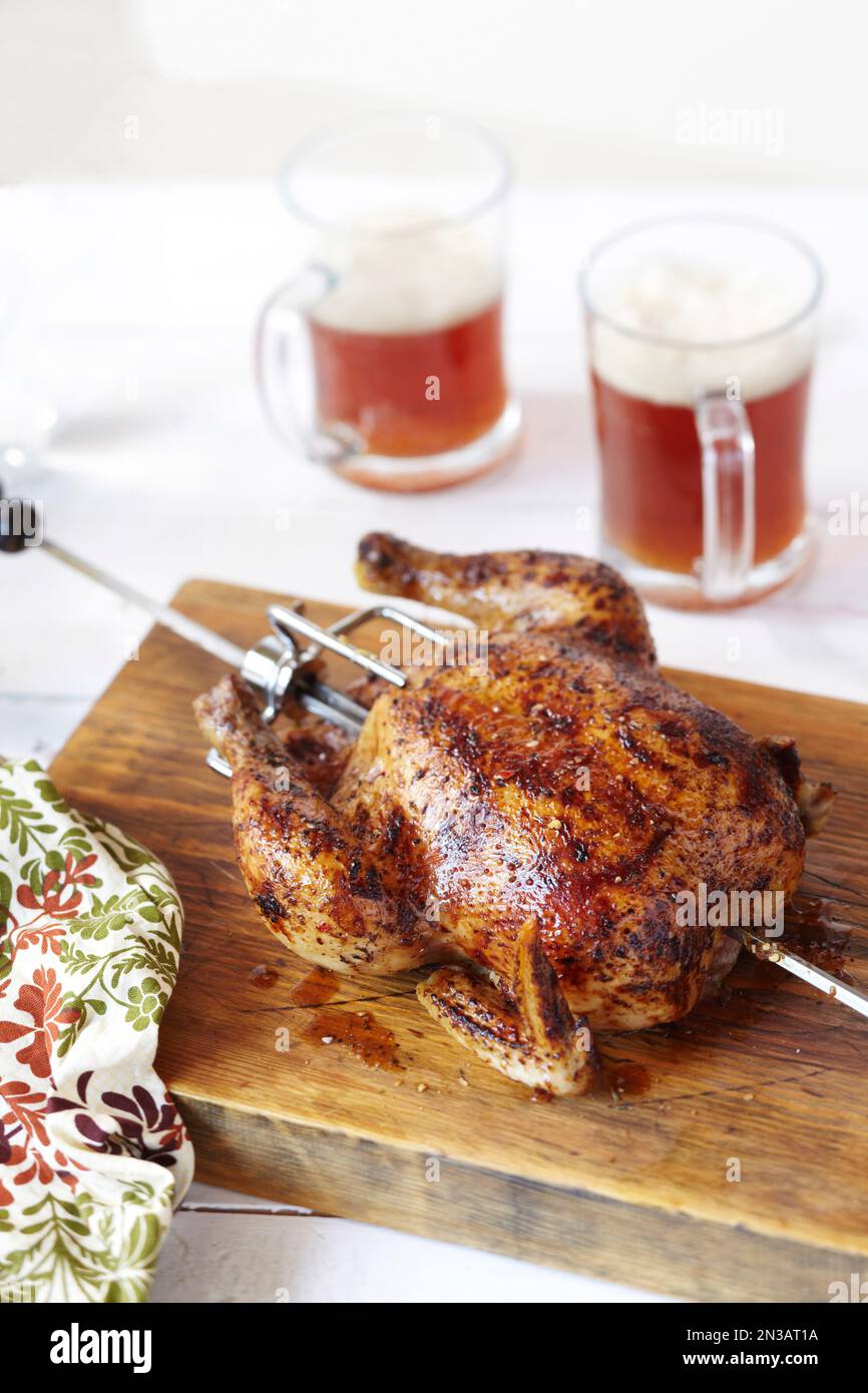 Whole chicken on rotisserie spit rod placed on cutting board with two ...