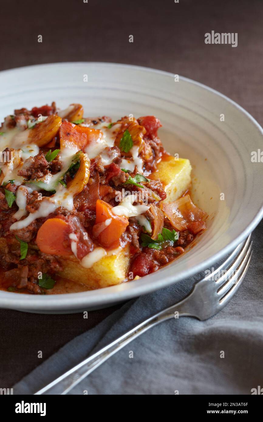 Bowl of beef stew served on a polenta wedge topped with melted ...