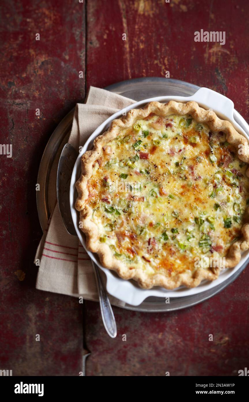 Whole quiche with ham and onions in baking dish on barnboard background ...