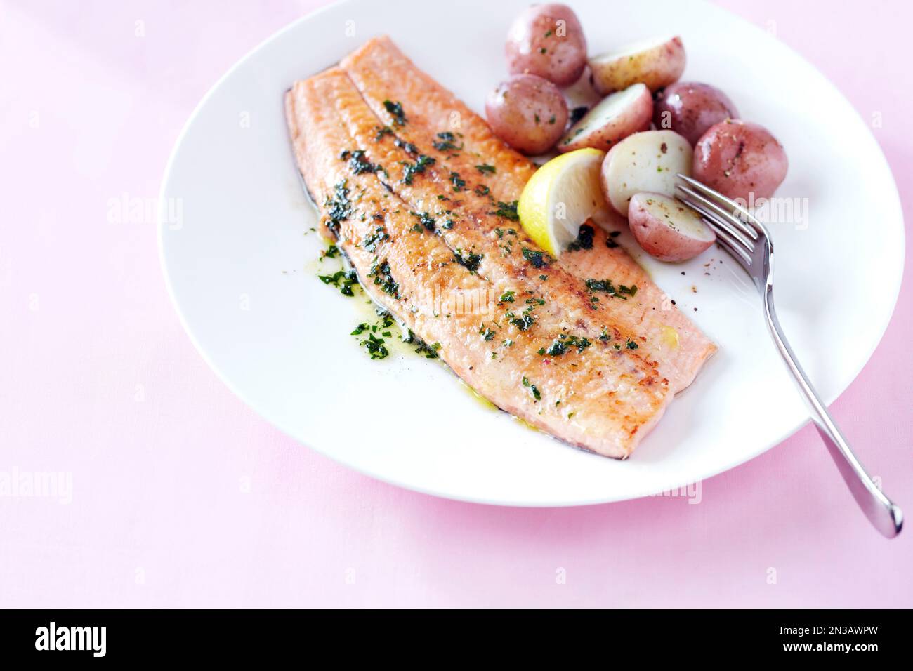 Fillet of trout with lemon herb butter and baby potatoes on a pink ...