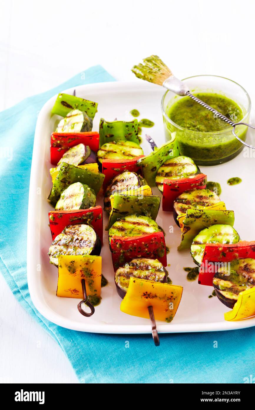Grilled vegetable skewers with pesto butter on a white platter with ...