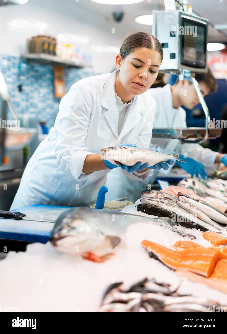 Positive saleswoman demonstrating seabass in fish store Stock Photo - Alamy