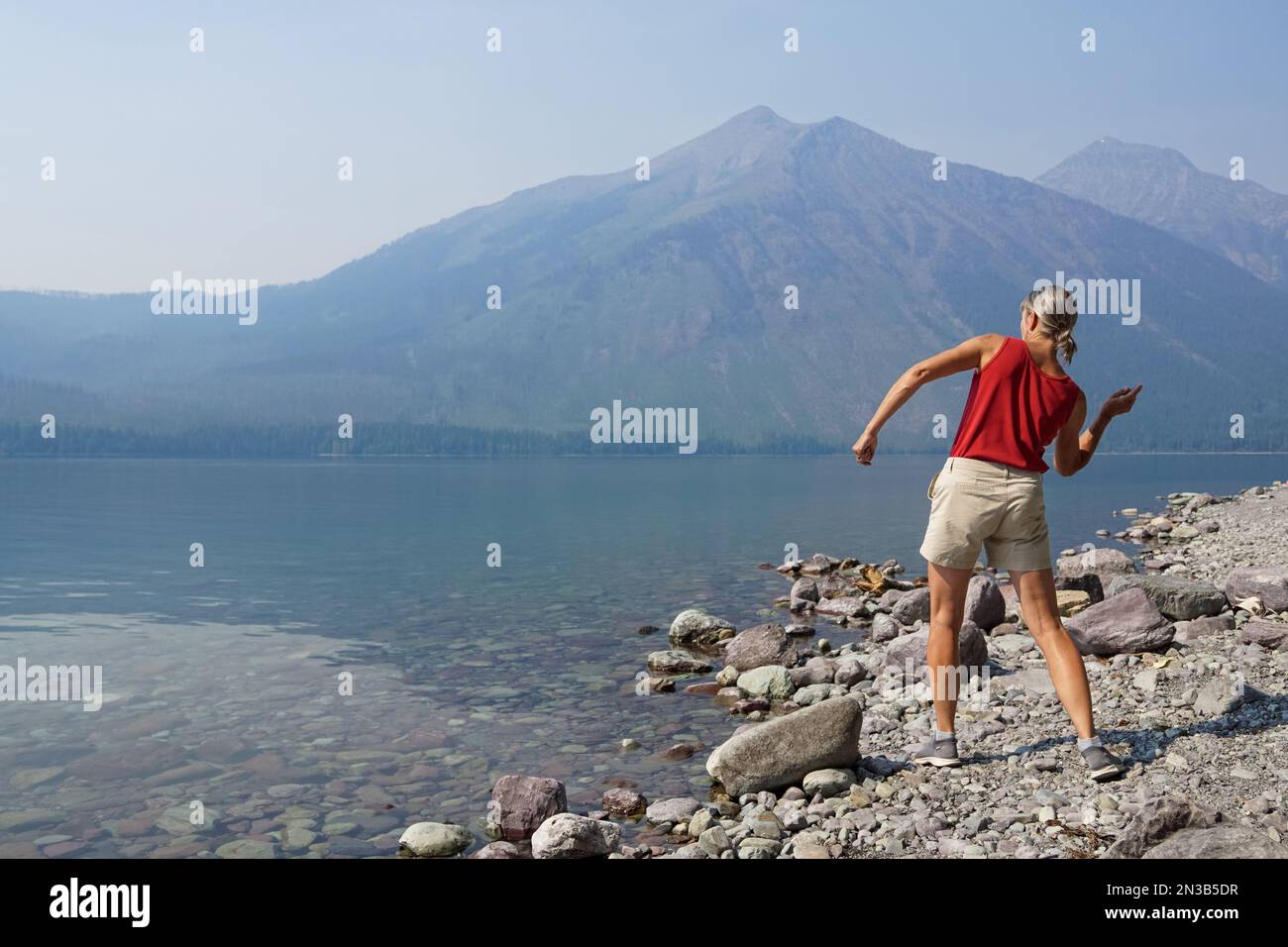 Woman throwing a rock in a lake with a mountain background Stock Photo ...