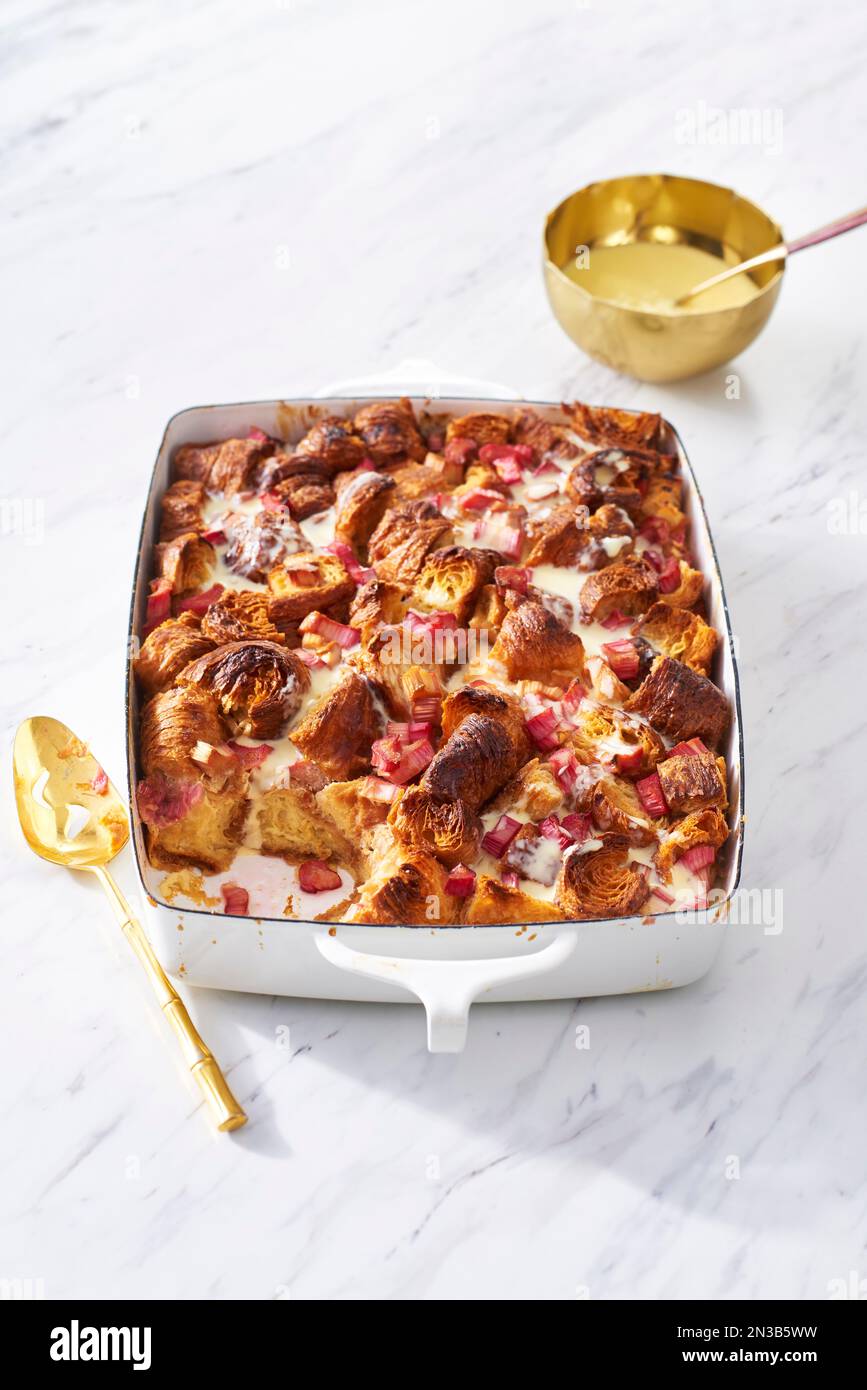 Rhubarb bread pudding in a casserole dish with gold serving spoon and a ...