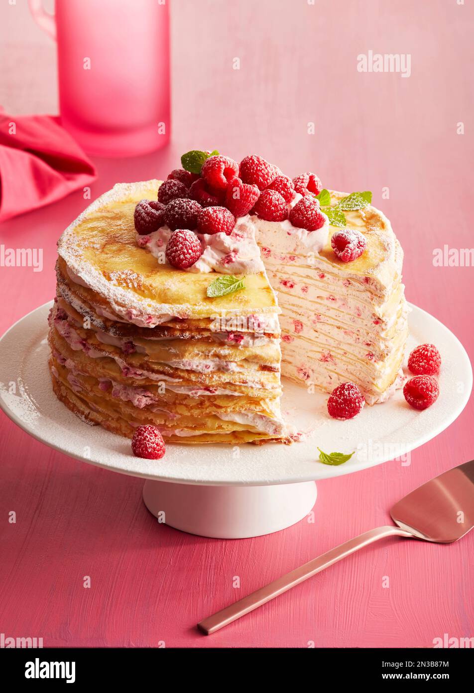 Raspberry crepe cake on a pedestal cake stand on a pink background ...