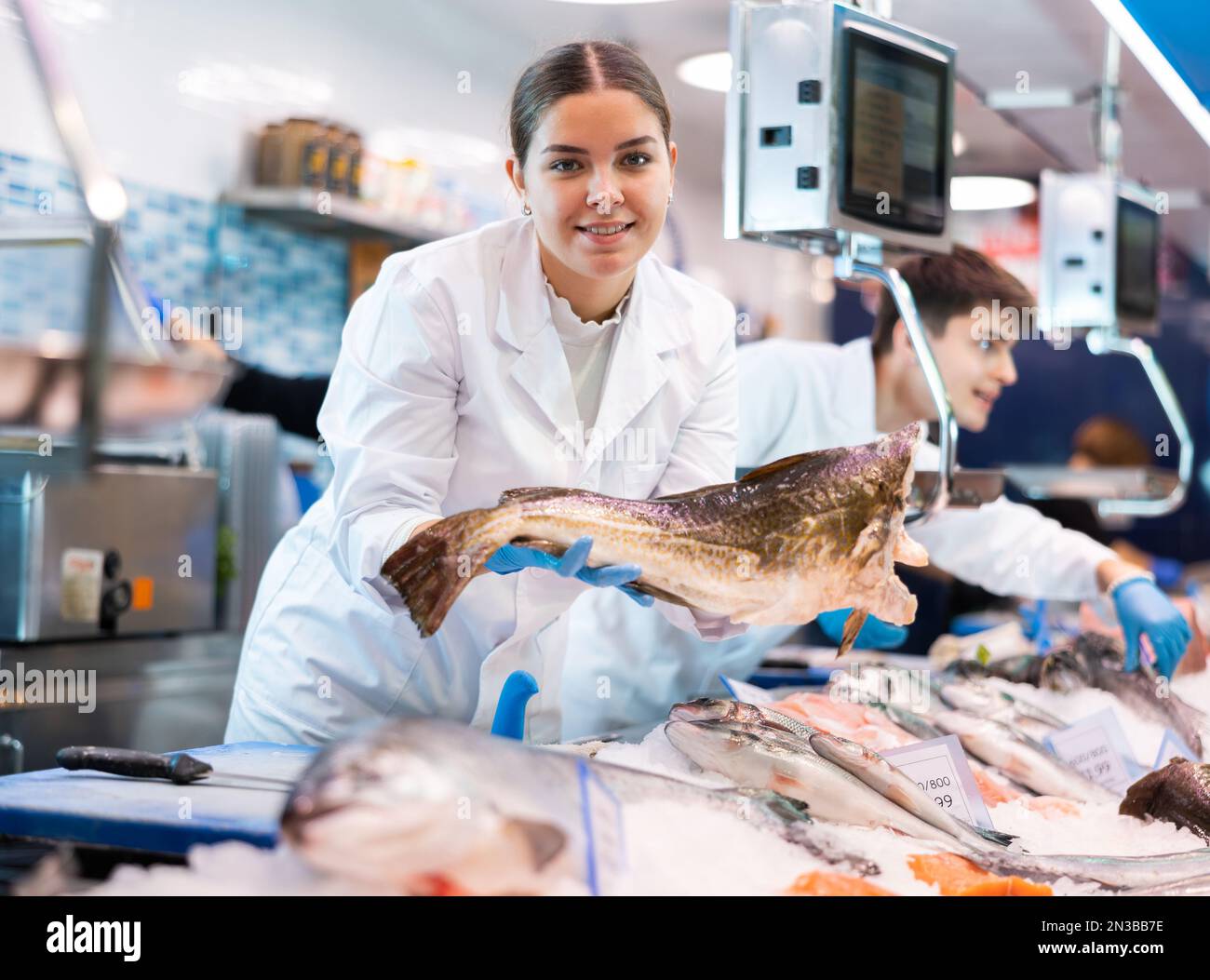 Positive saleswoman holding cod fish in fish store Stock Photo - Alamy