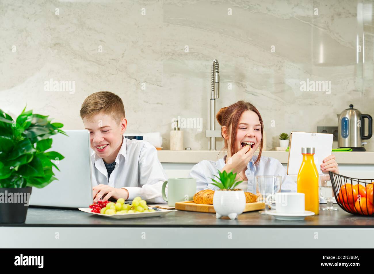 Happy childrens, kids having breakfast at home and using digital devices. kids playing and ...