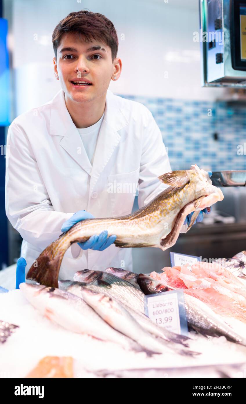 Positive salesman demonstrating cod in fish store Stock Photo - Alamy