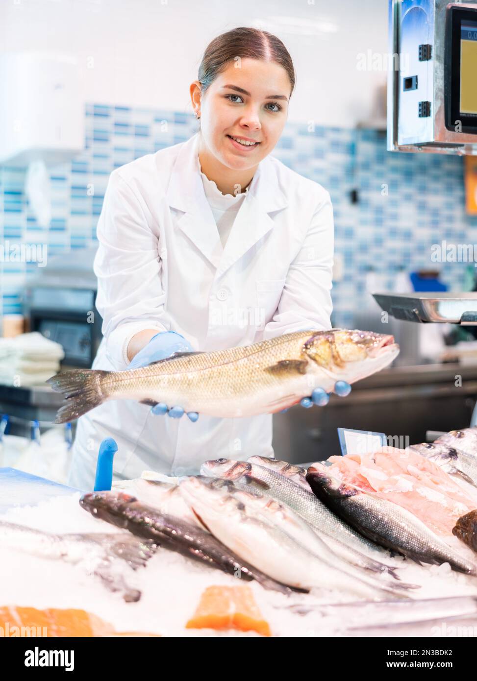 Positive saleswoman demonstrating seabass in fish store Stock Photo - Alamy