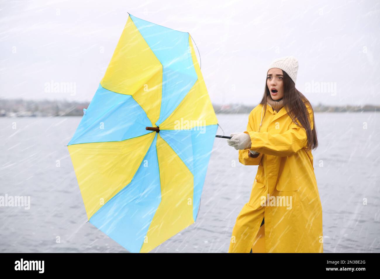 Woman in yellow raincoat with umbrella caught in gust of wind near ...