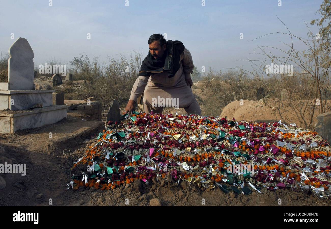 Pakistani gravedigger Taj Muhammad adjusts wreaths on a grave during ...
