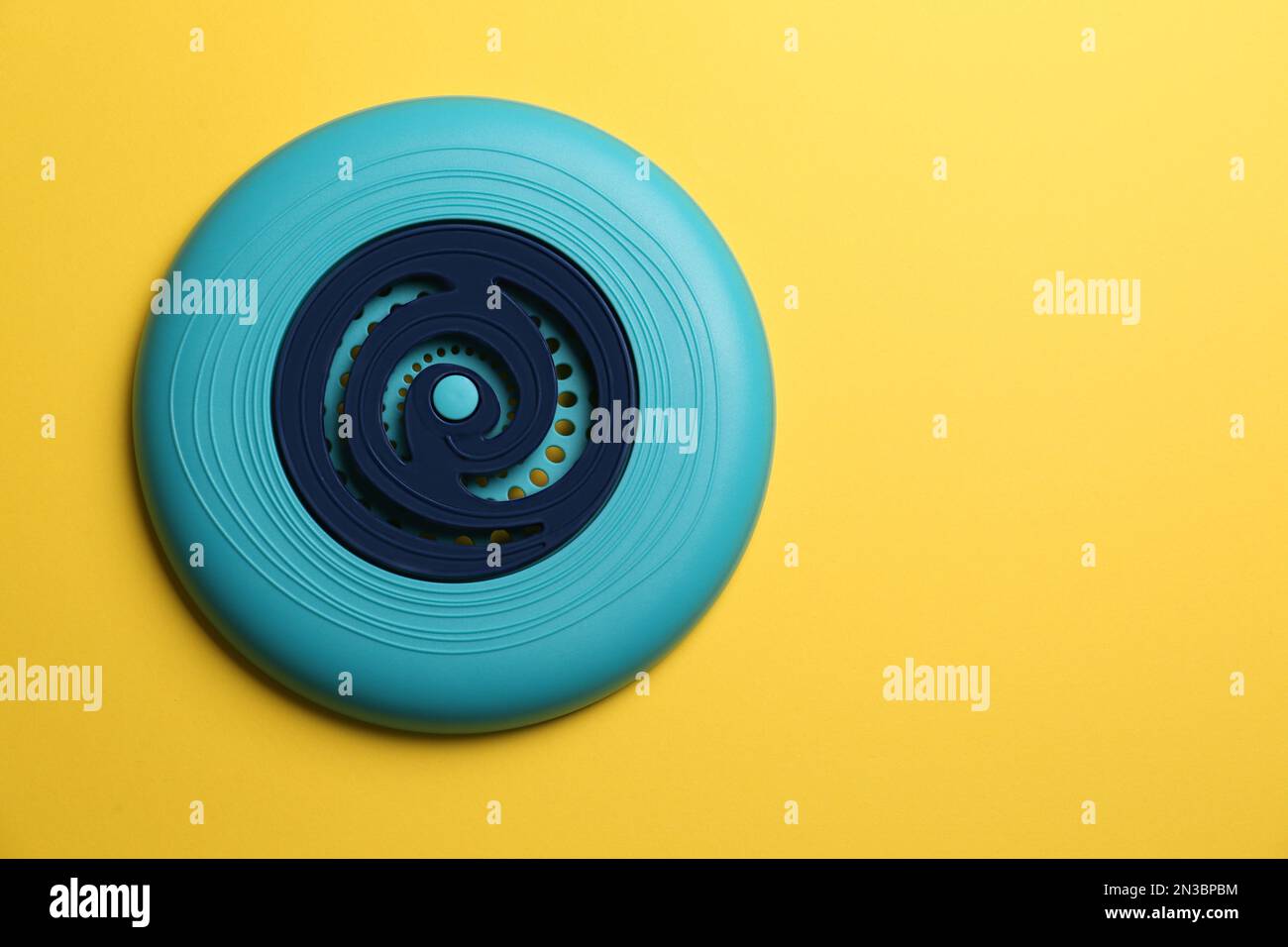 Blue plastic frisbee disk on yellow background, top view. Space for ...