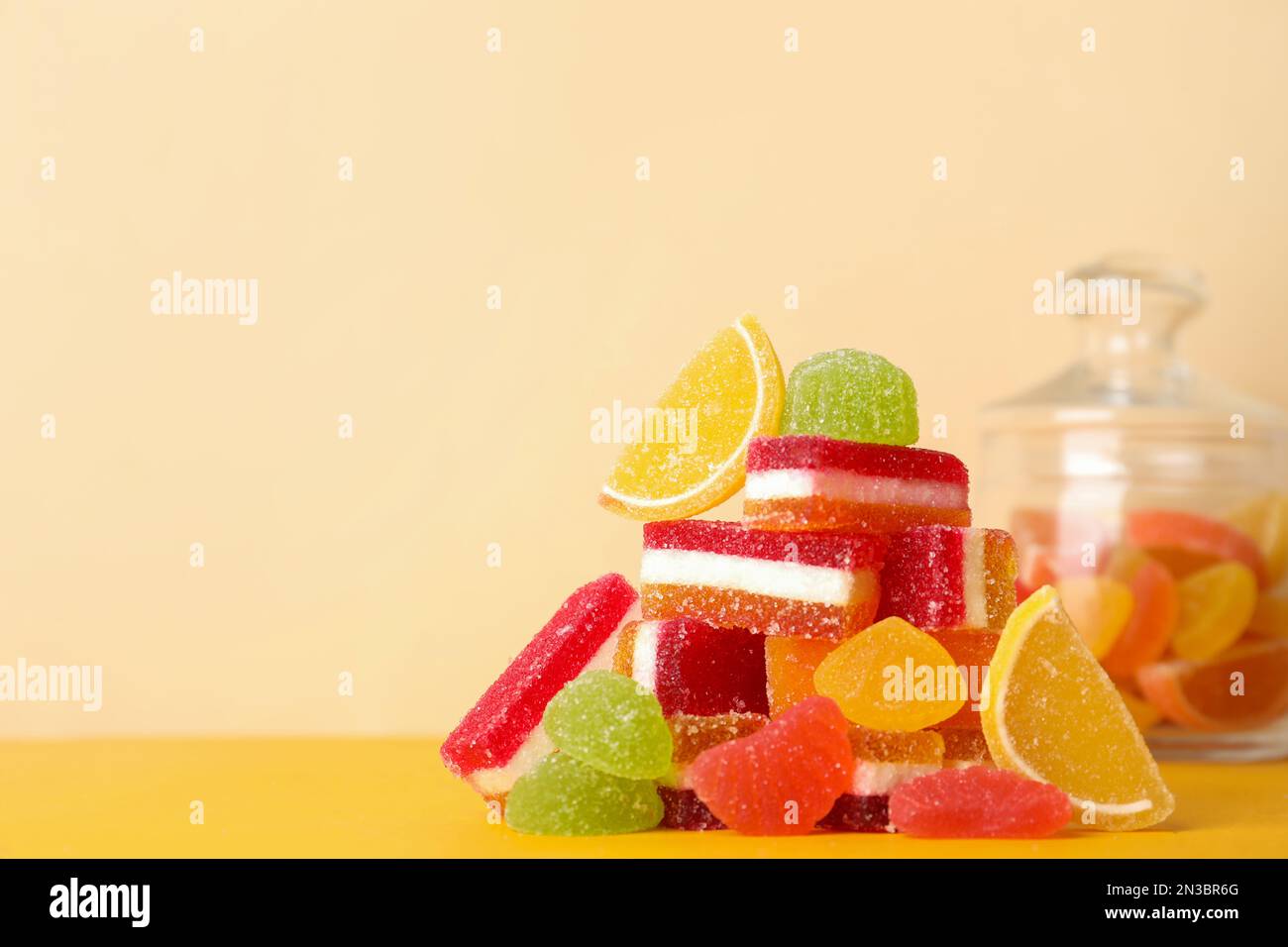 Pile of delicious bright jelly candies on yellow table. Space for text ...