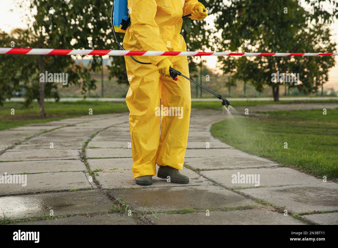 Person in hazmat suit disinfecting street pavement with sprayer ...
