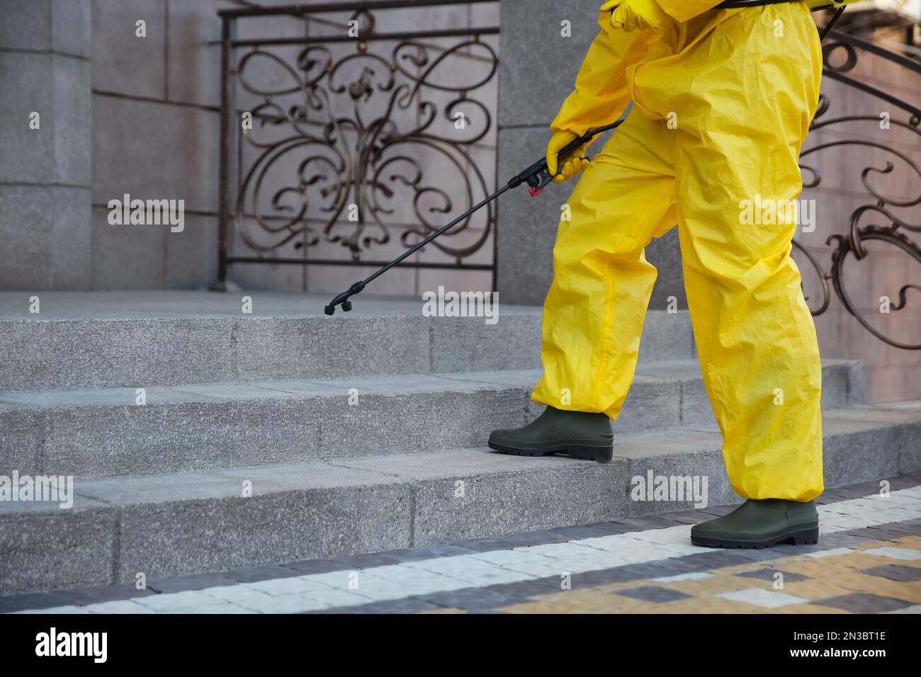 Person in hazmat suit disinfecting stairs with sprayer outdoors ...