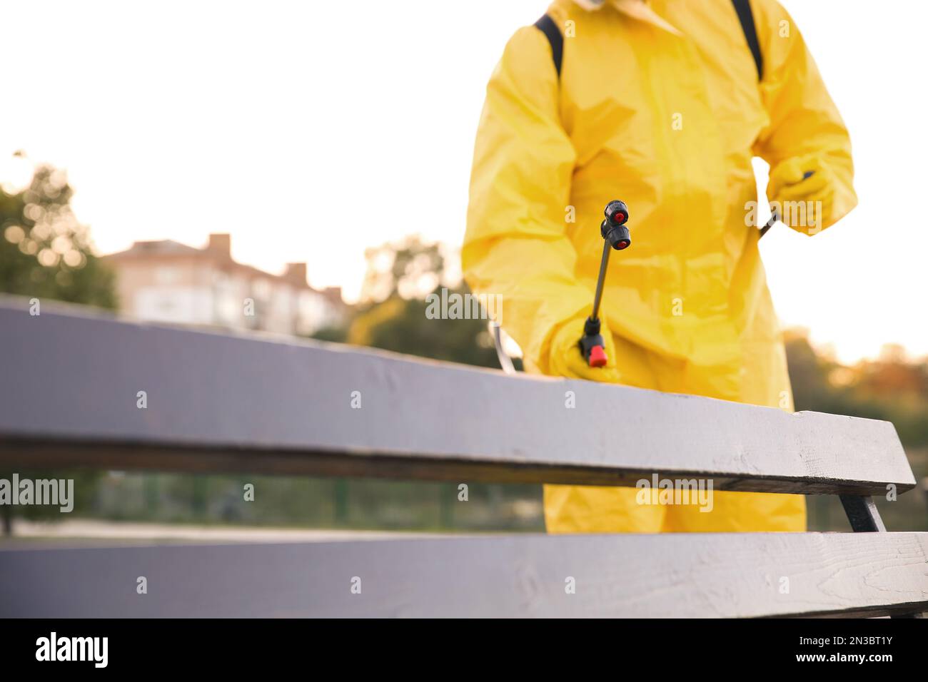 Person in hazmat suit disinfecting bench in park with sprayer, closeup ...