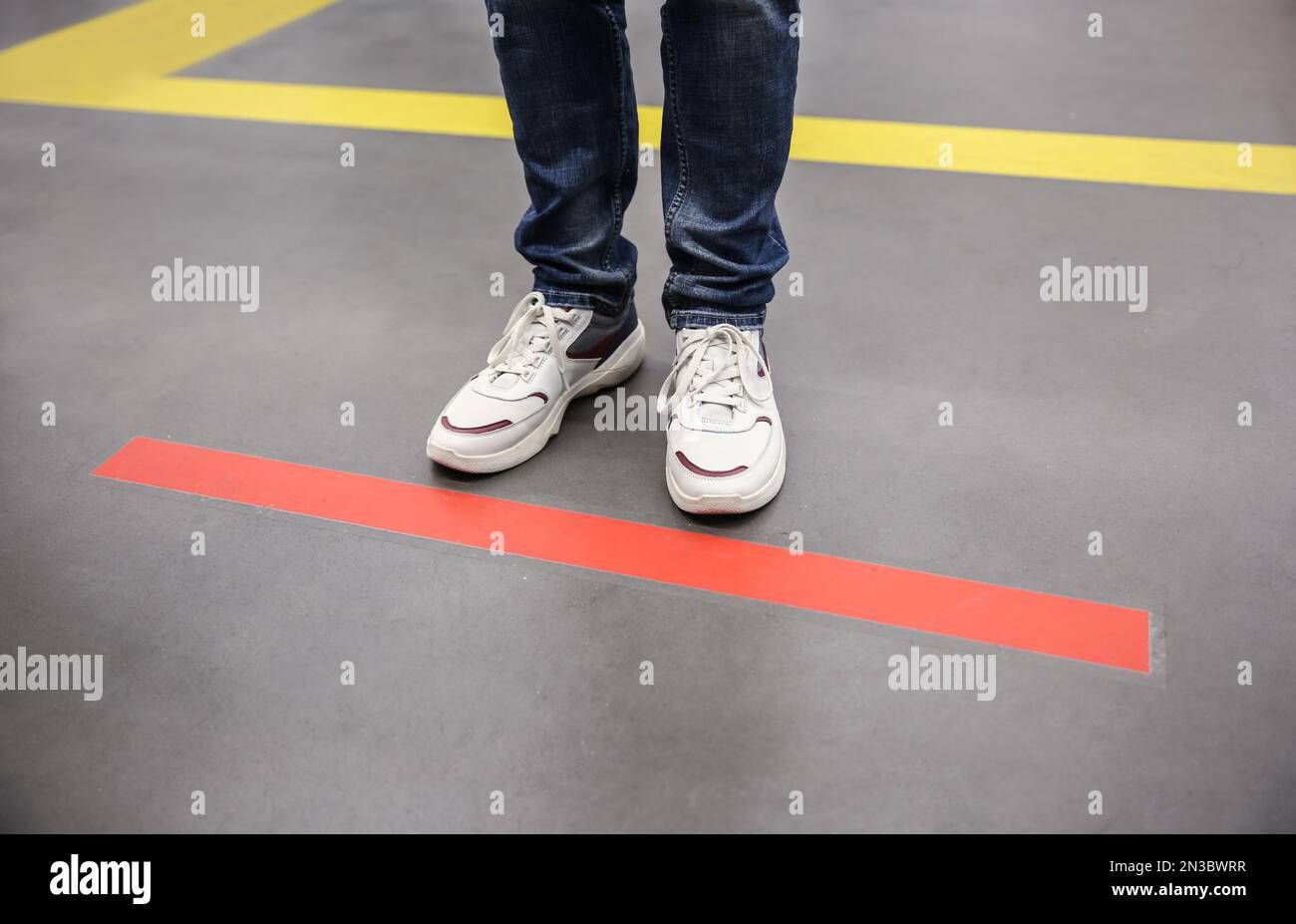 Person standing behind taped floor marking indoors for social distance ...