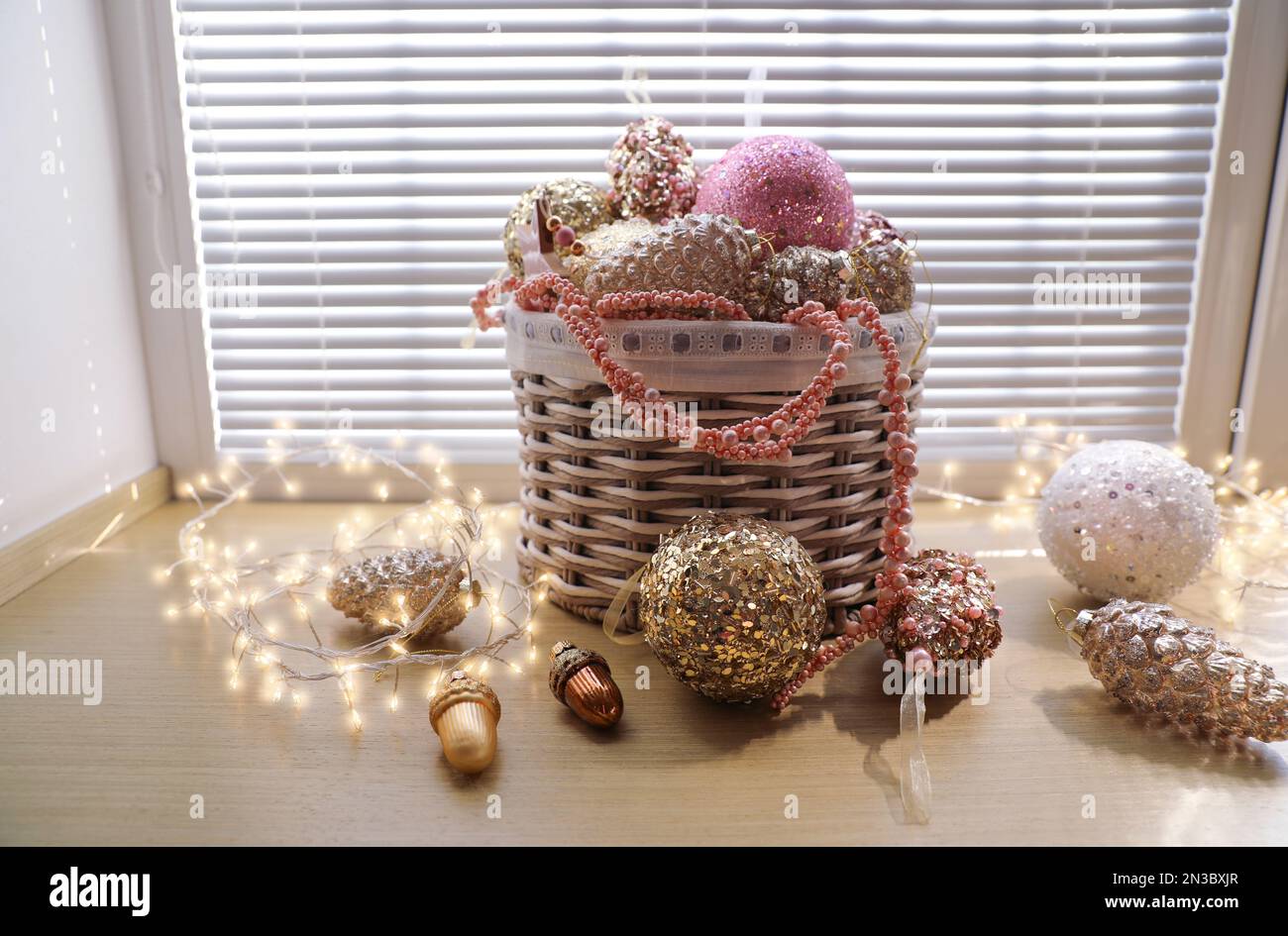 Basket with beautiful Christmas tree baubles and fairy lights on window ...