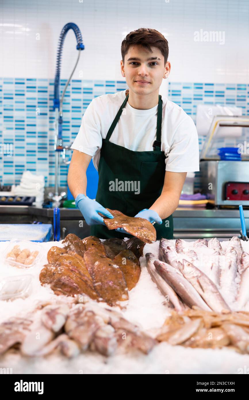 Positive salesman demonstrating sole fish behind counter in shop Stock ...