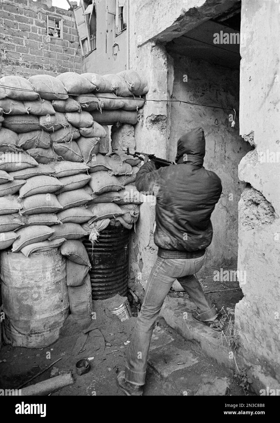 A hooded Muslim sniper fires his gun through a small opening in a sand ...