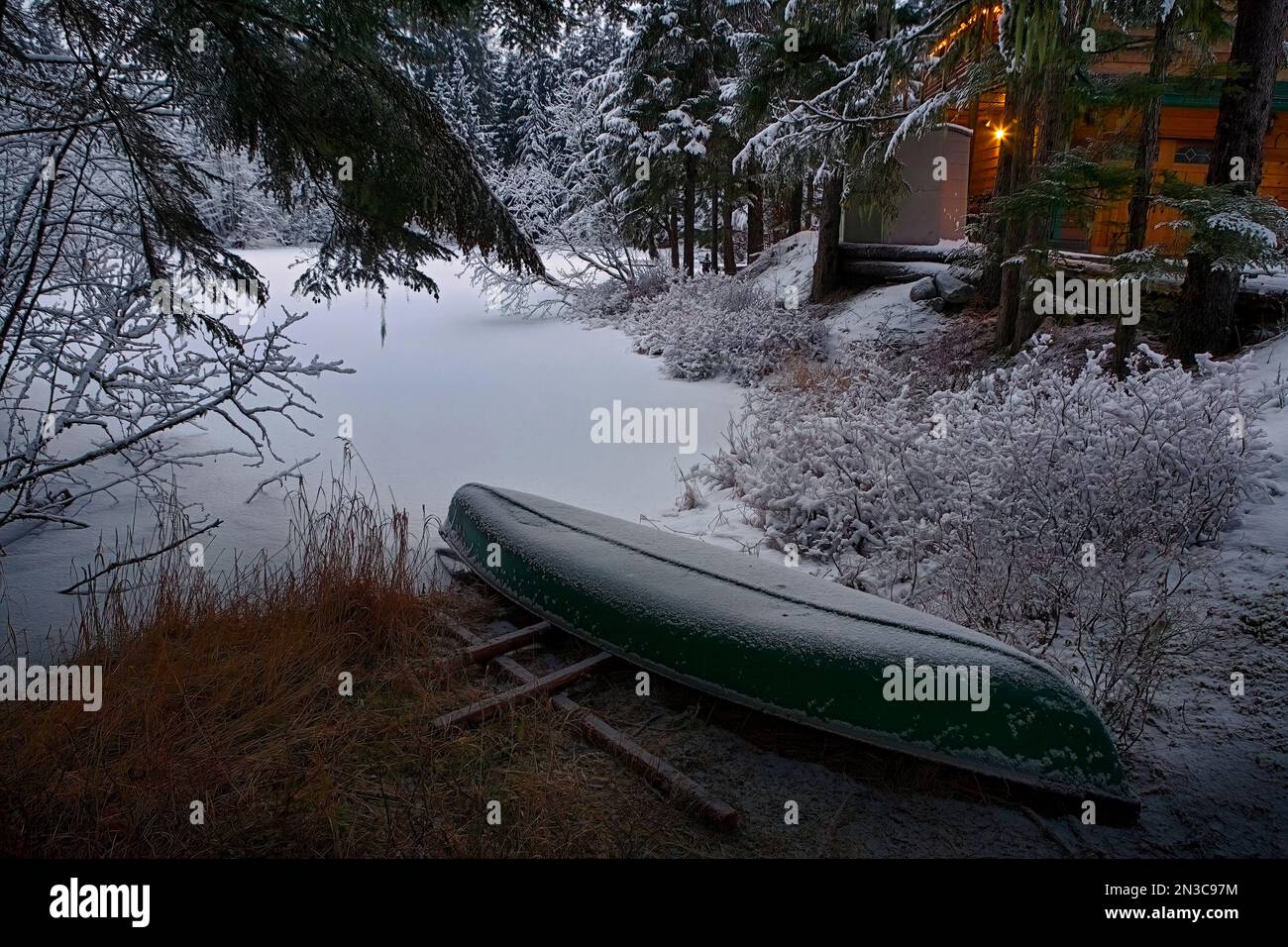 Frosty morning snow on a beached canoe and trees surrounding a small ...