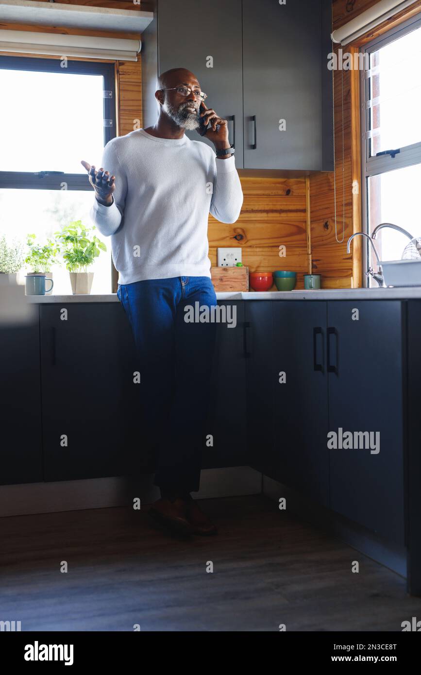 Bald african american senior man talking over mobile phone by kitchen ...