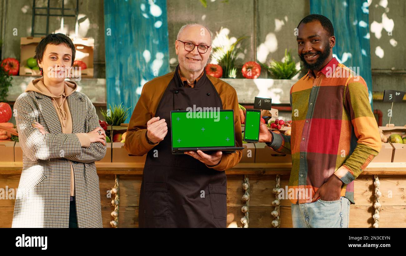 Diverse group of people showing greenscreen on laptop and smartphone ...