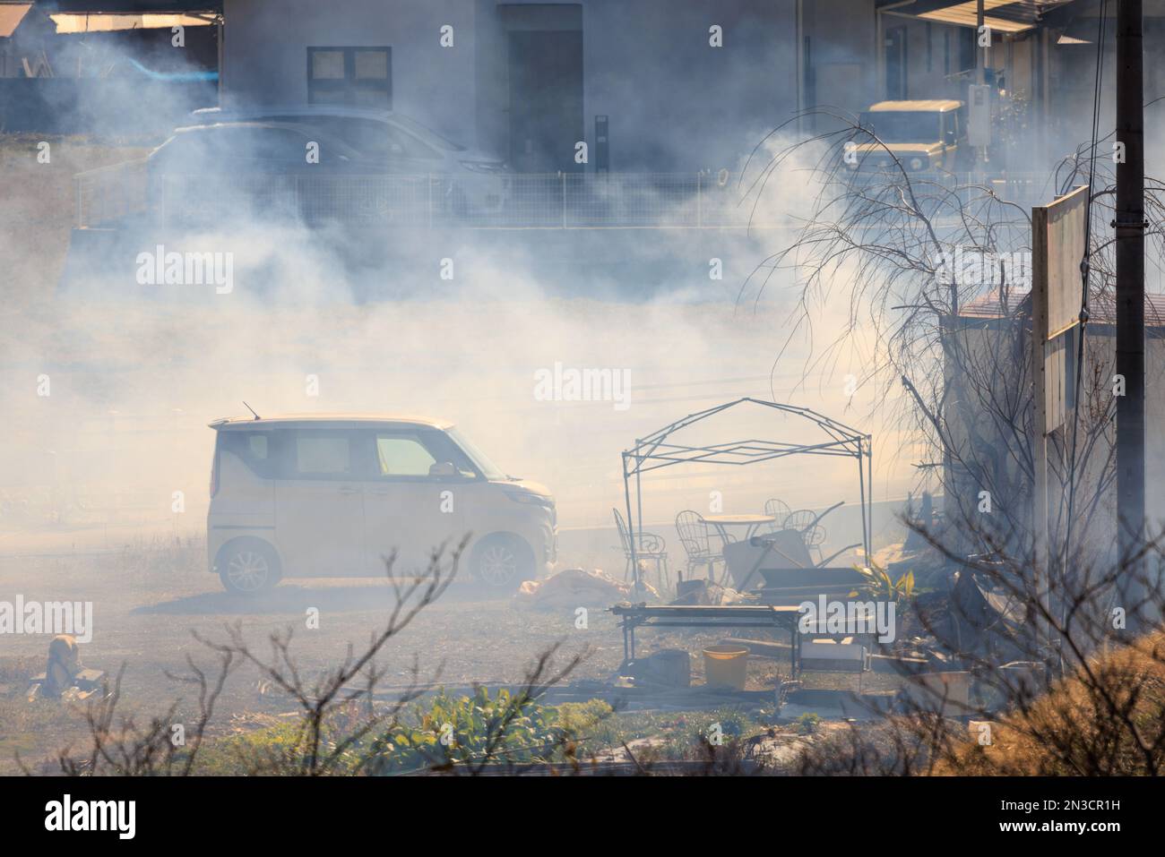 Thick smoke around small car on suburban yard with garden furniture ...