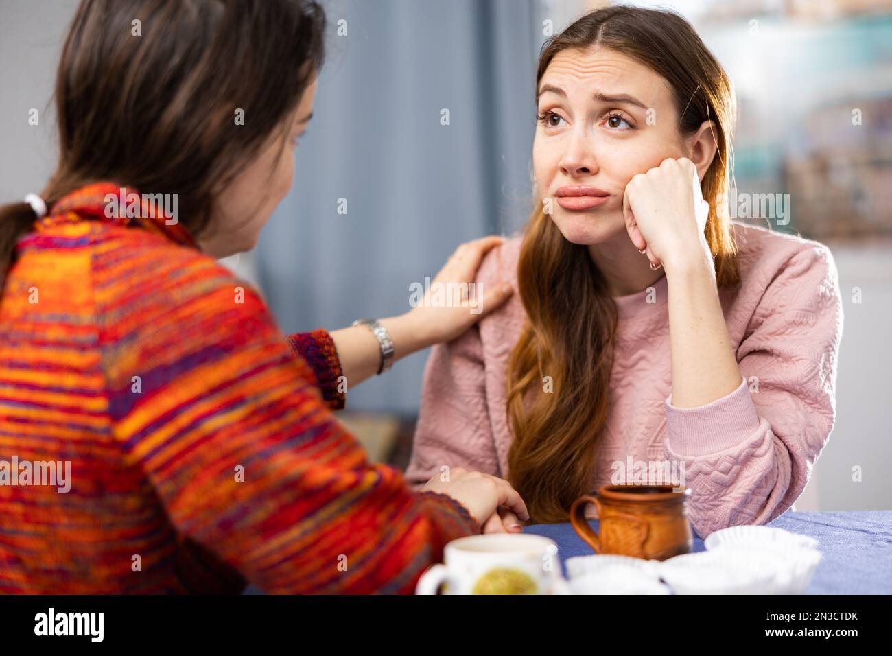 Sad woman sitting at table with her friend who supporting her Stock ...