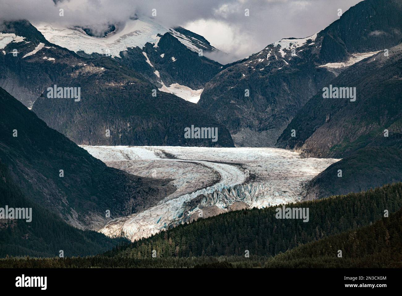 Massive, glacial flow of the Eagle Glacier surrounded by snow-capped mountains under a cloudy ...