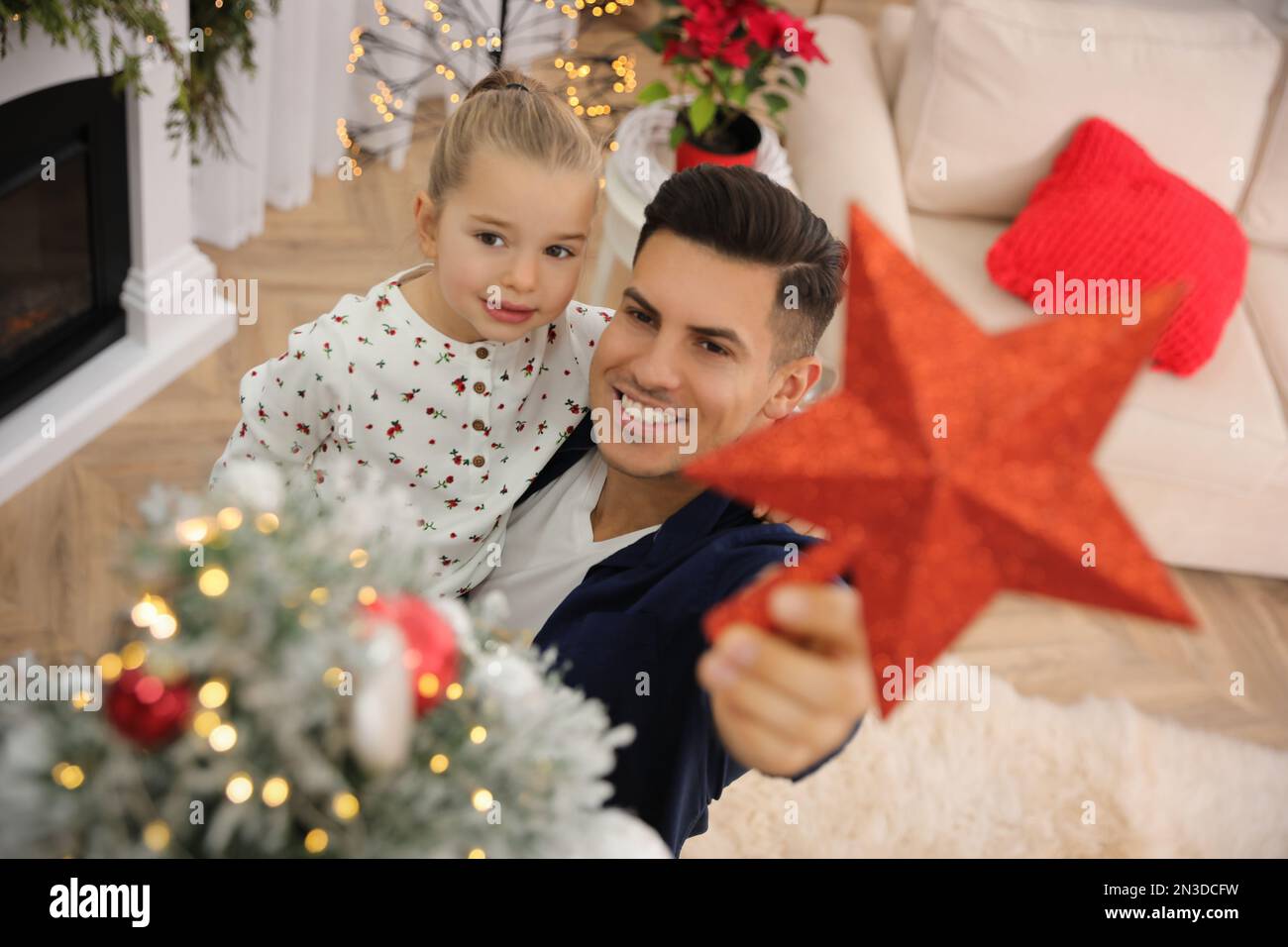 Father and little daughter decorating Christmas tree with star topper ...