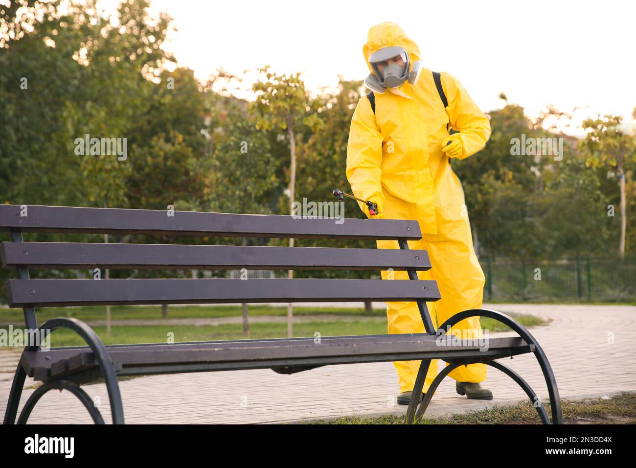 Person in hazmat suit disinfecting bench in park with sprayer. Surface ...