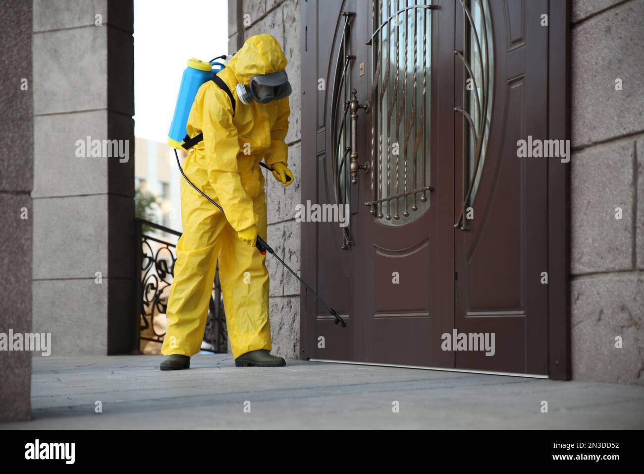 Person in hazmat suit disinfecting entrance door with sprayer. Surface ...