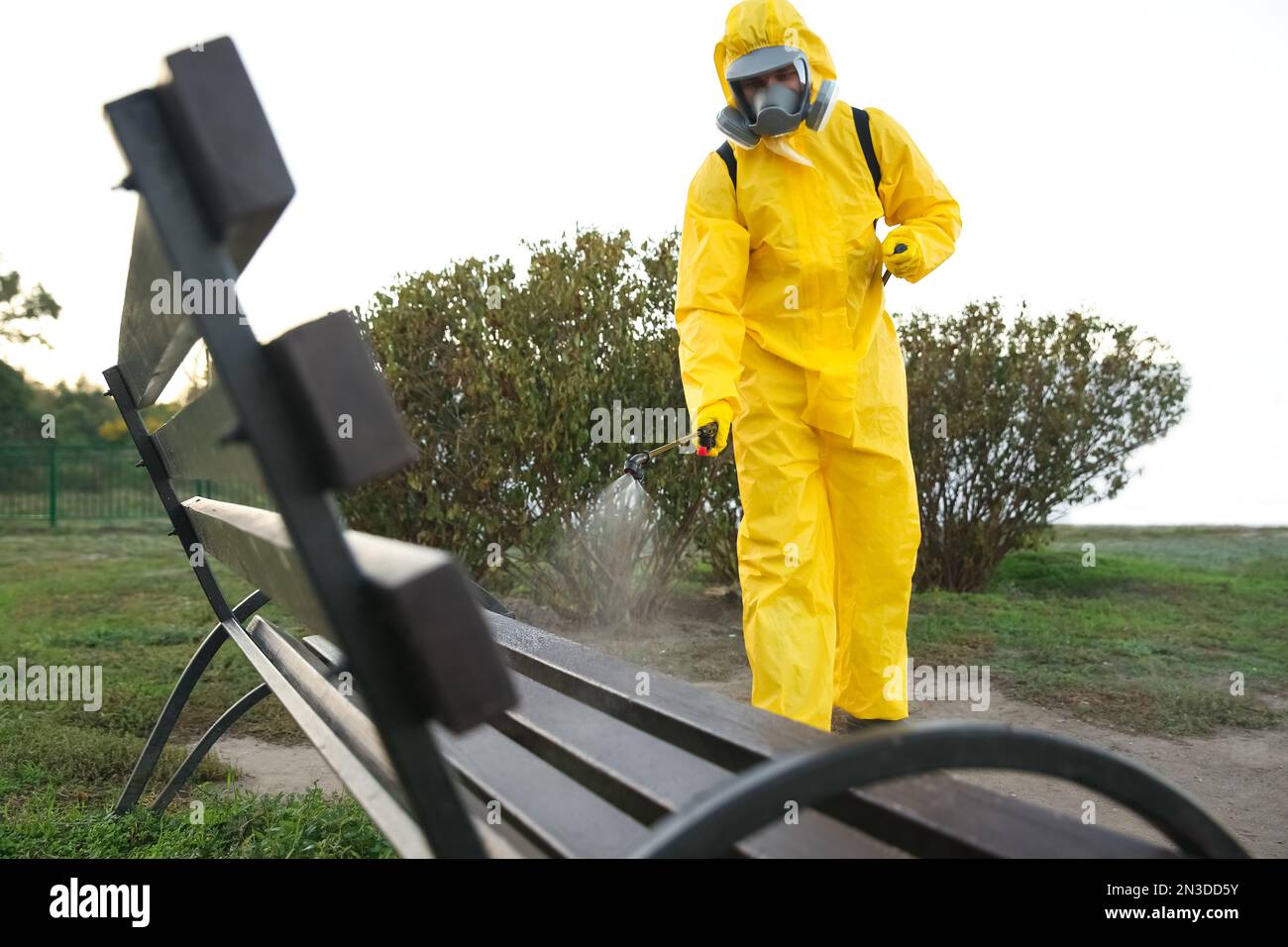 Person in hazmat suit disinfecting bench in park with sprayer. Surface ...