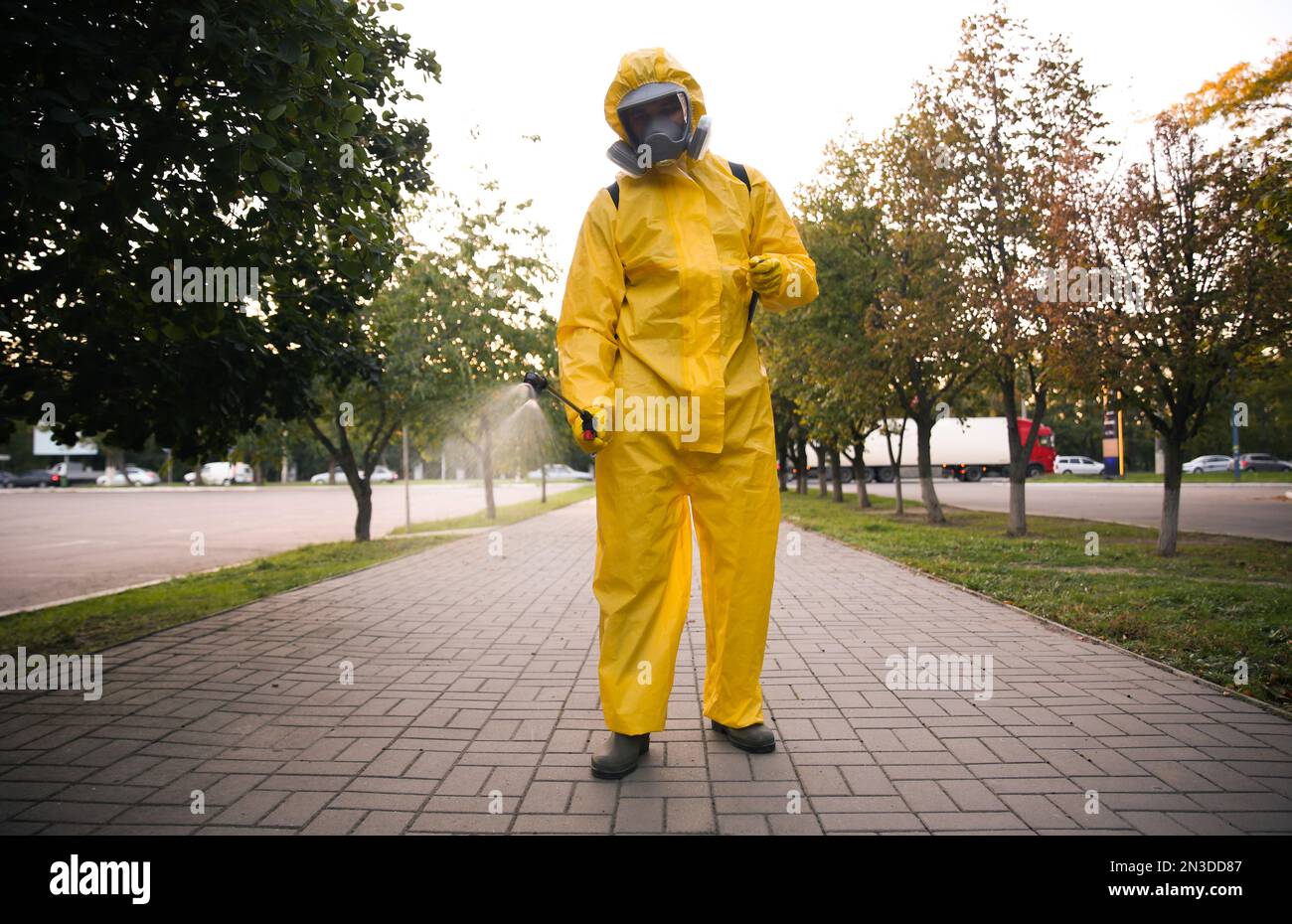 Person in hazmat suit disinfecting street pavement with sprayer ...