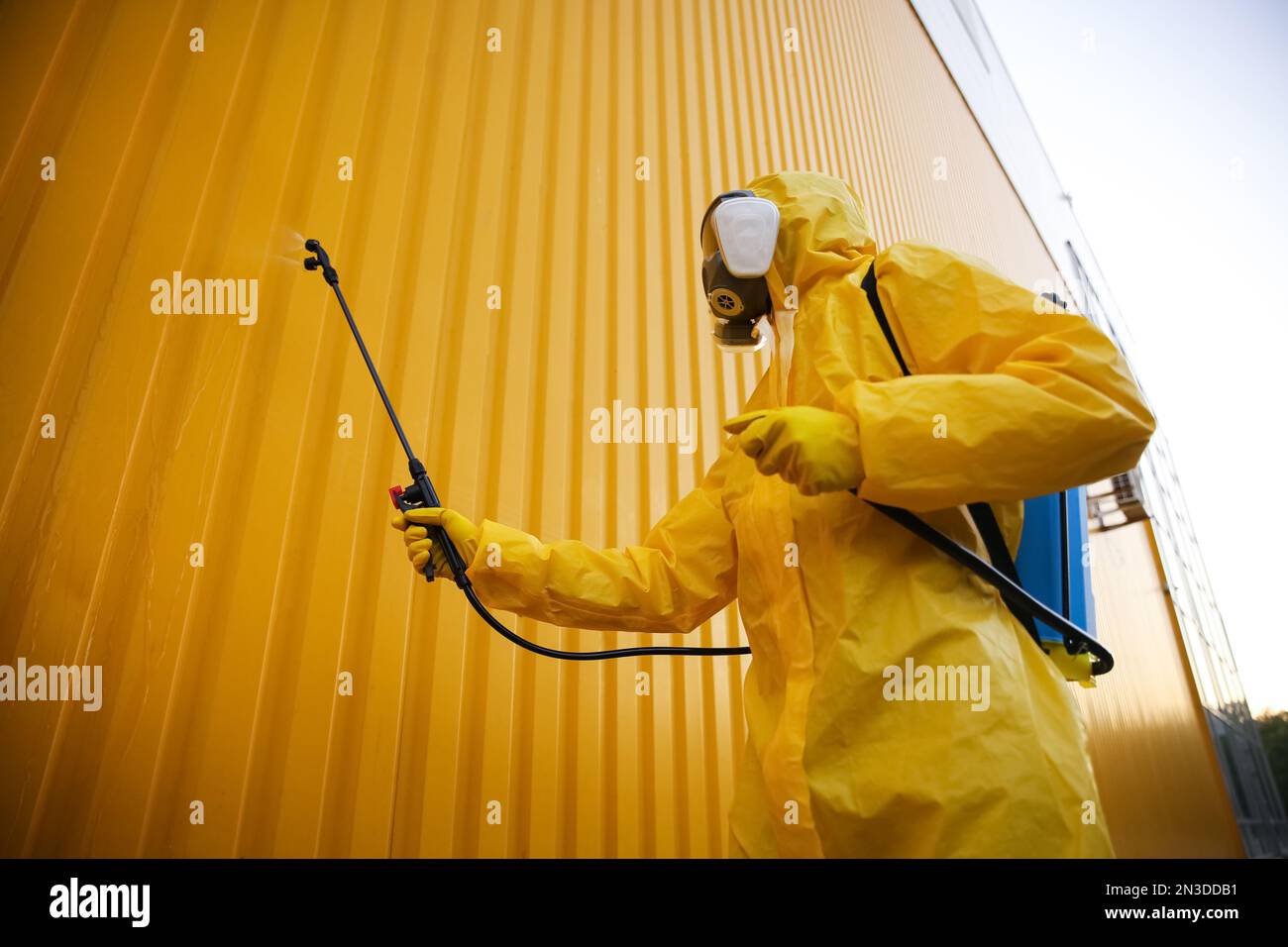 Person in hazmat suit disinfecting building wall with sprayer outdoors ...