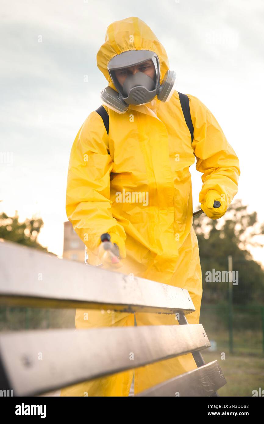 Person in hazmat suit disinfecting bench in park with sprayer. Surface ...