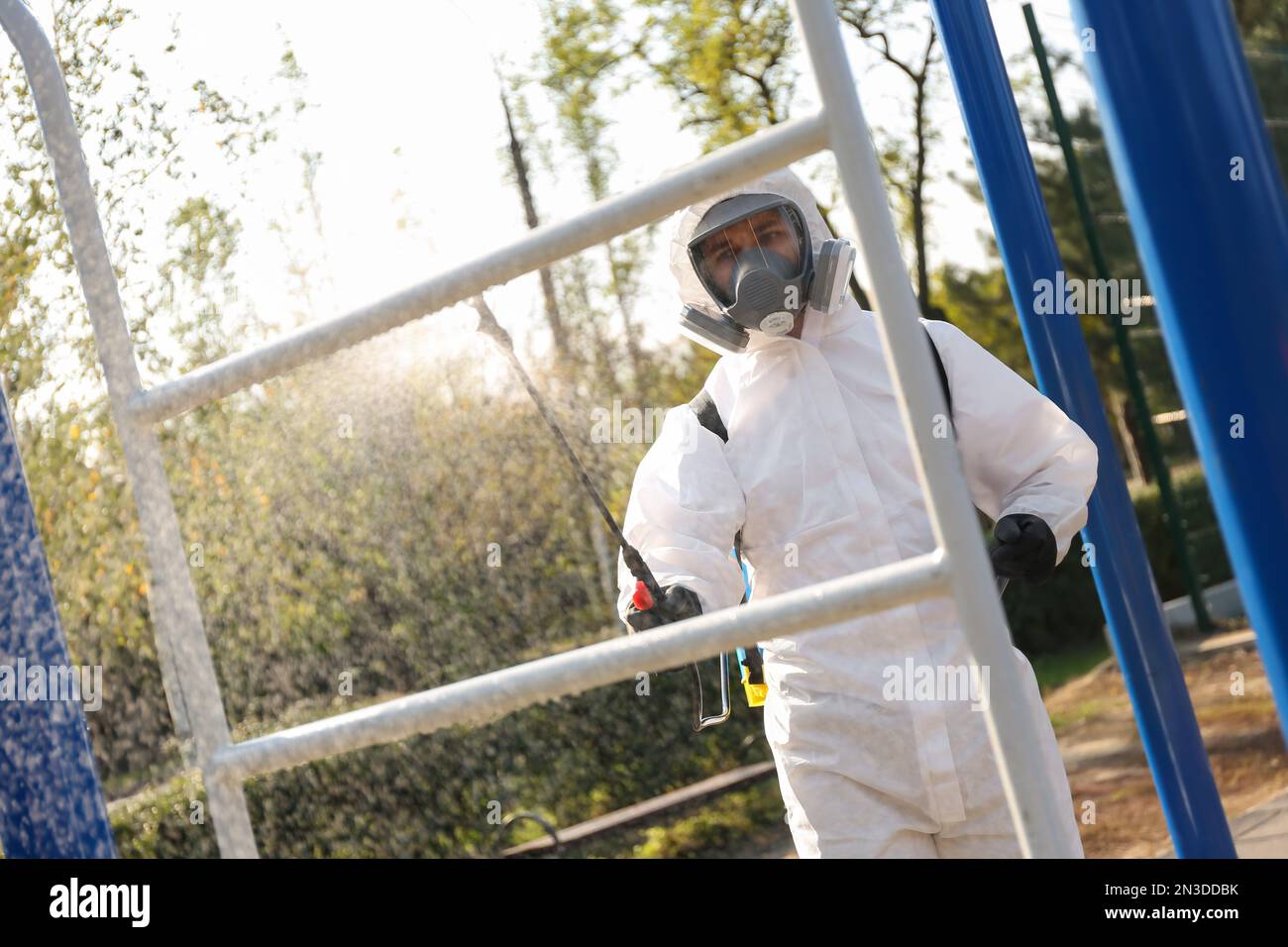 Man in hazmat suit spraying disinfectant on outdoor gym's equipment ...